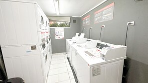 Uma lavanderia com várias máquinas de lavar e secar, terminais de pagamento e cartazes informativos nas paredes.