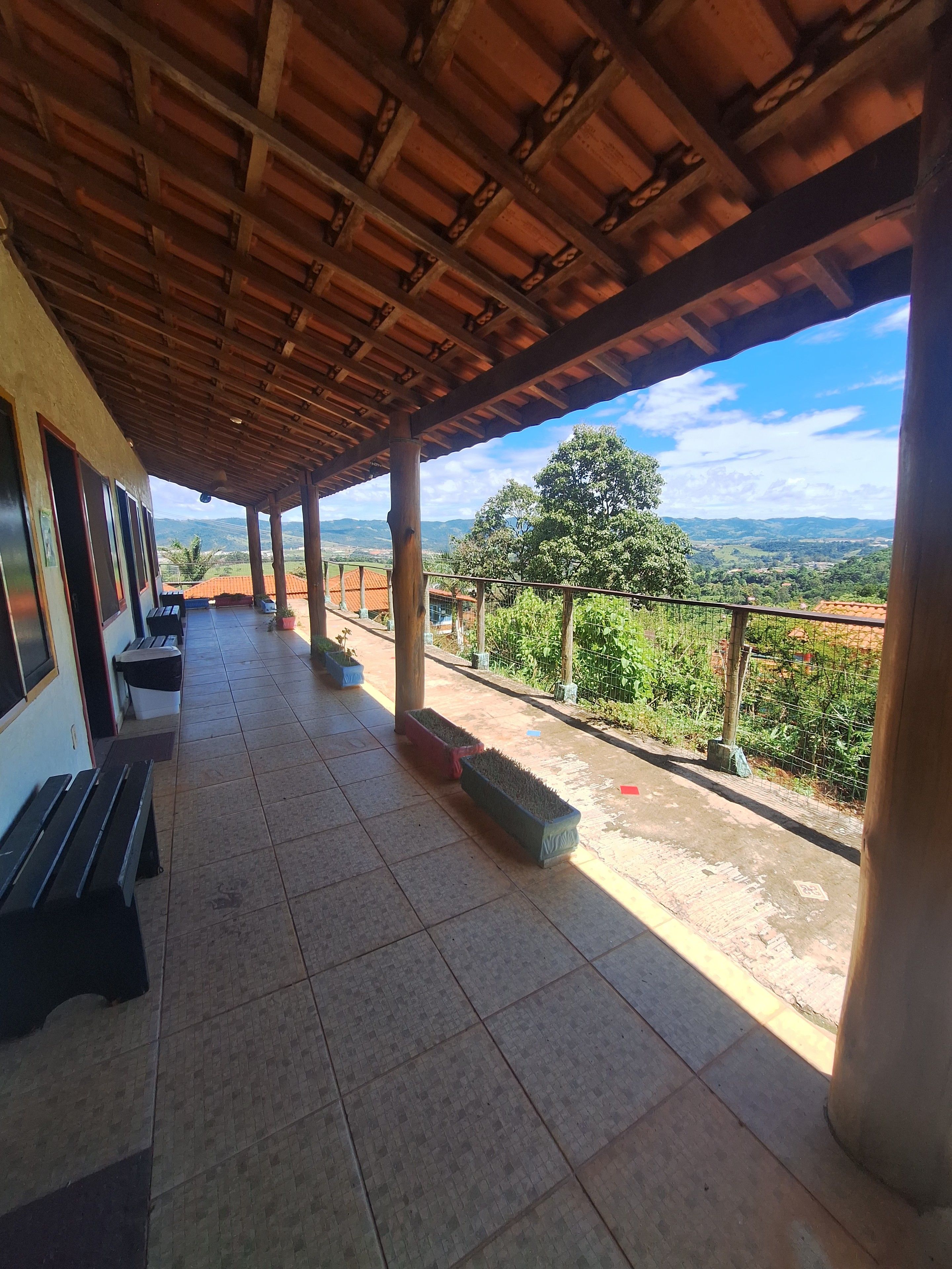 Área externa coberta com piso de azulejos, bancos e vista para a paisagem.
