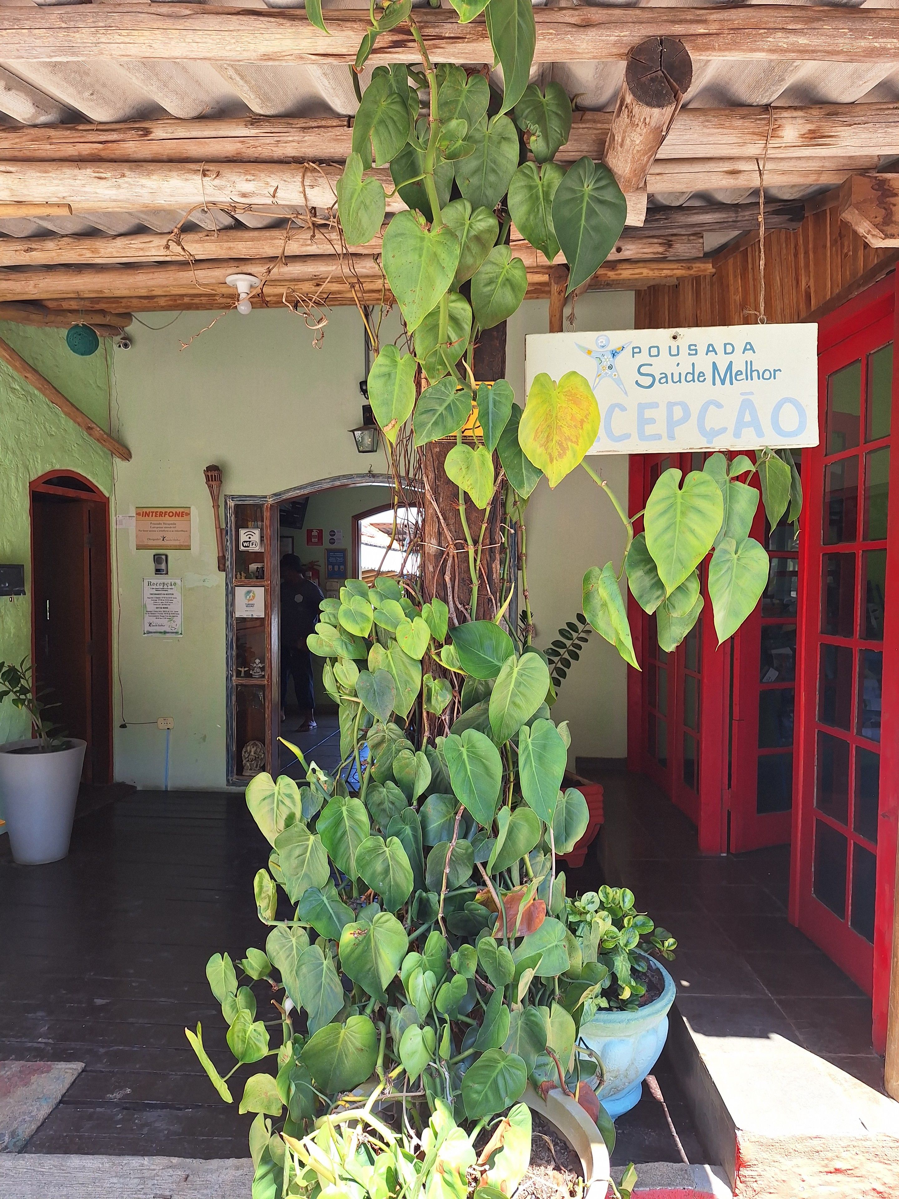 Uma área de recepção com uma placa indicando 'Pousada Saúde Melhor' e teto de madeira.