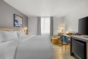 Quarto de hotel com uma cama grande, uma escrivaninha, uma cadeira, uma televisão e um quadro na parede.