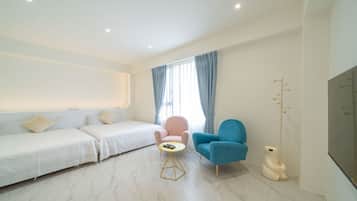 Quarto de hotel moderno com sofá, duas cadeiras, uma mesinha e TV.