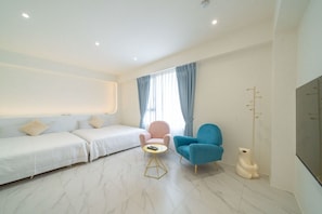 Quarto de hotel moderno com sofá, duas cadeiras, uma mesinha e TV.