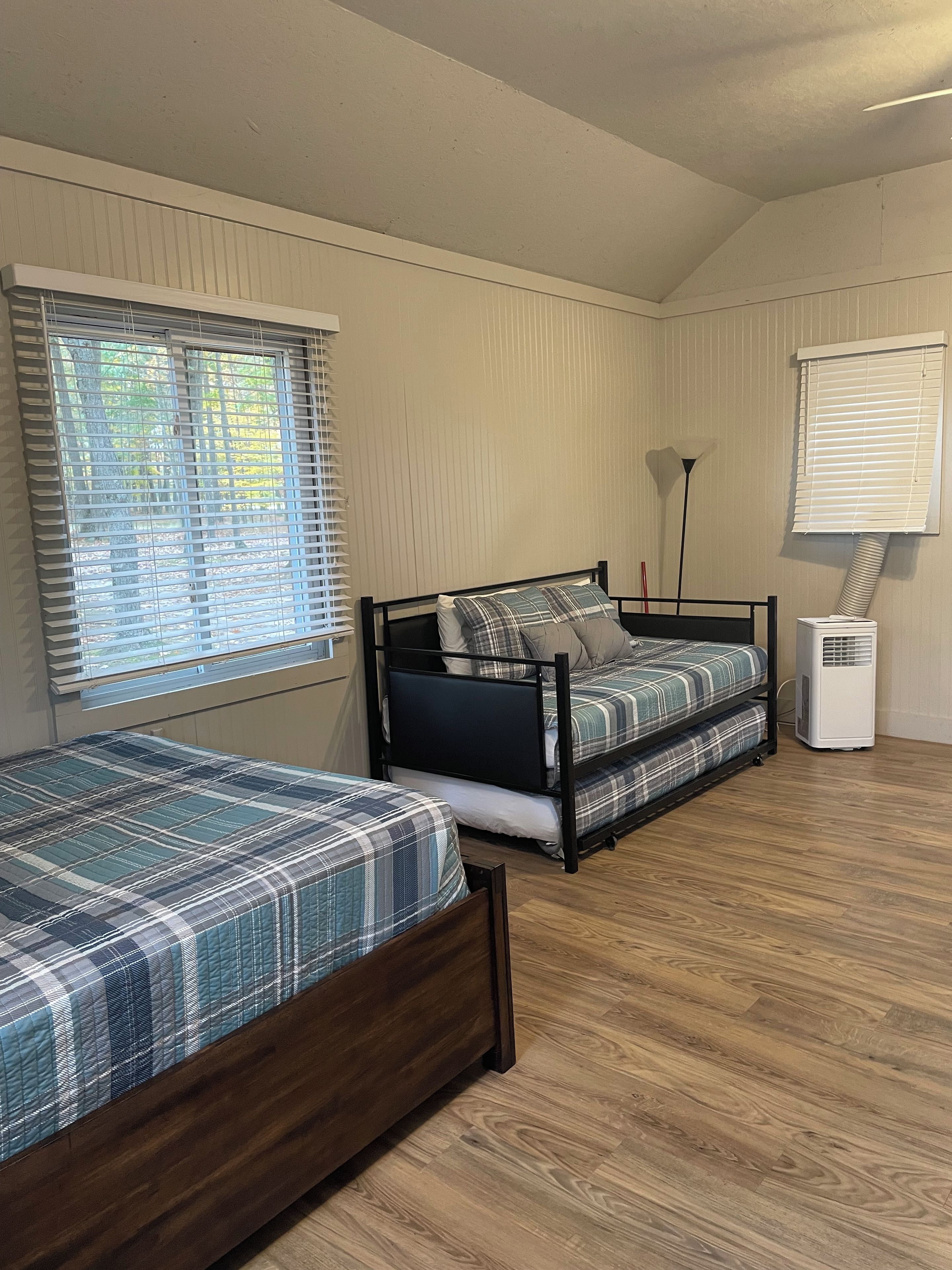 Quarto com duas camas, aquecedor portátil e janela com persianas.