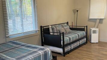 Quarto com duas camas, aquecedor portátil e janela com persianas.