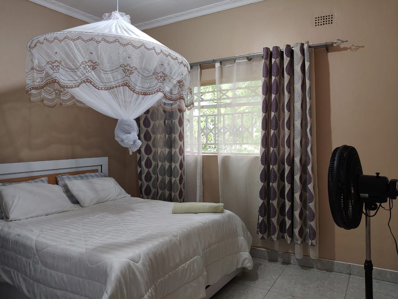 Quarto com cama, ventoinha de cabeceira e janela com cortinas.