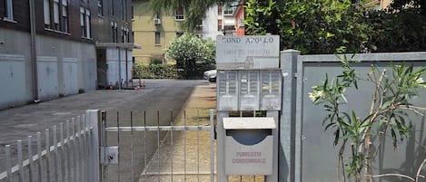 Portão fechado para uma área residencial, com uma placa indicando 'COND. APOLLO' e 'CORSO DEL POPOLO 146'.