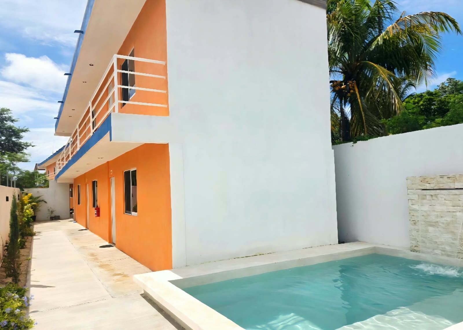 Um edifício de dois andares com fachada laranja, piscina e parede branca com detalhes em pedra.