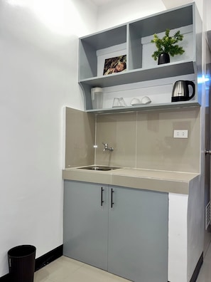 Cozinha compacta com pia, armários e uma prateleira com utensílios de cozinha.