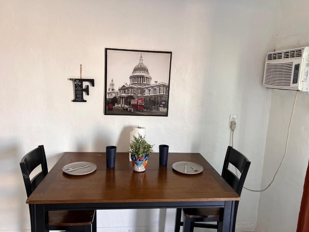 Uma mesa de jantar com cadeiras, um quadro com a imagem de um edifício, a letra 'F' e um aparelho de ar condicionado.