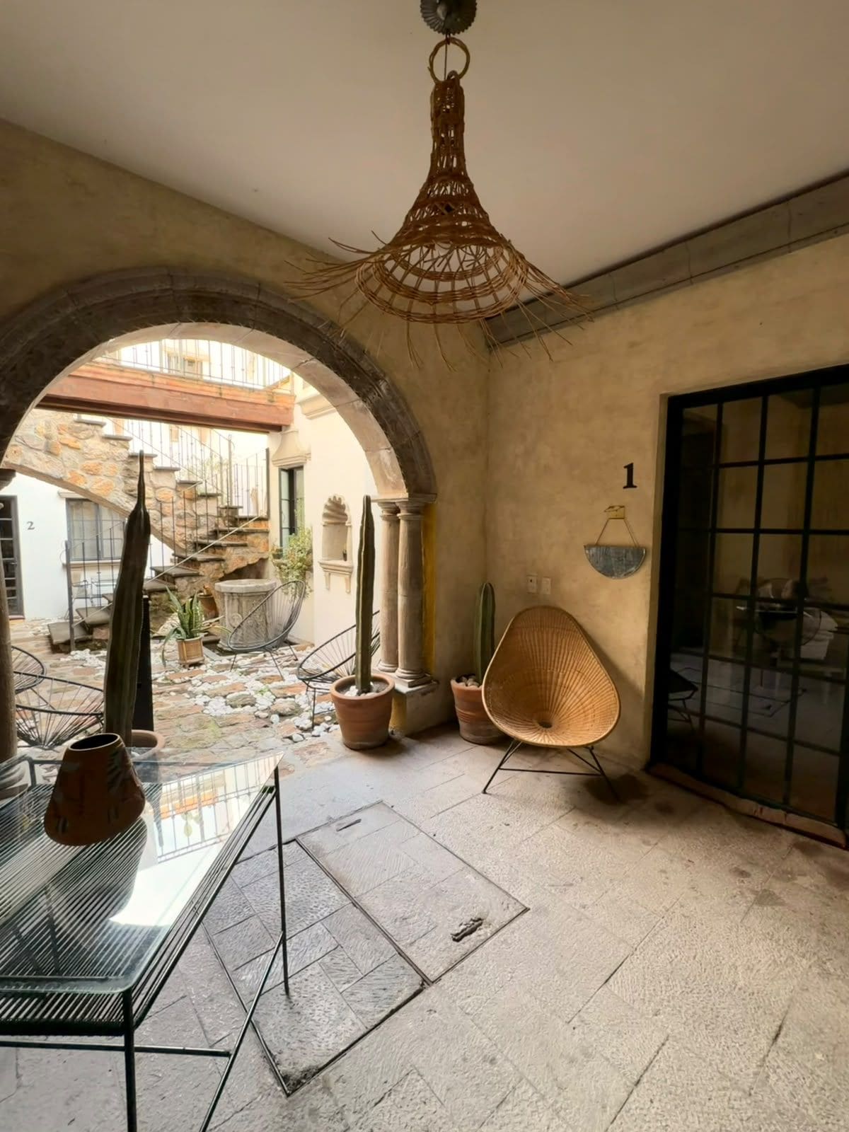 Um pátio externo com mesa, cadeiras, plantas em vasos e um lustre pendurado.
