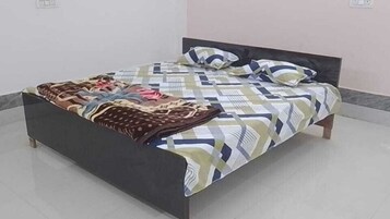 Uma cama com colcha estampada e almofadas, cabeceira escura e chão de azulejos.