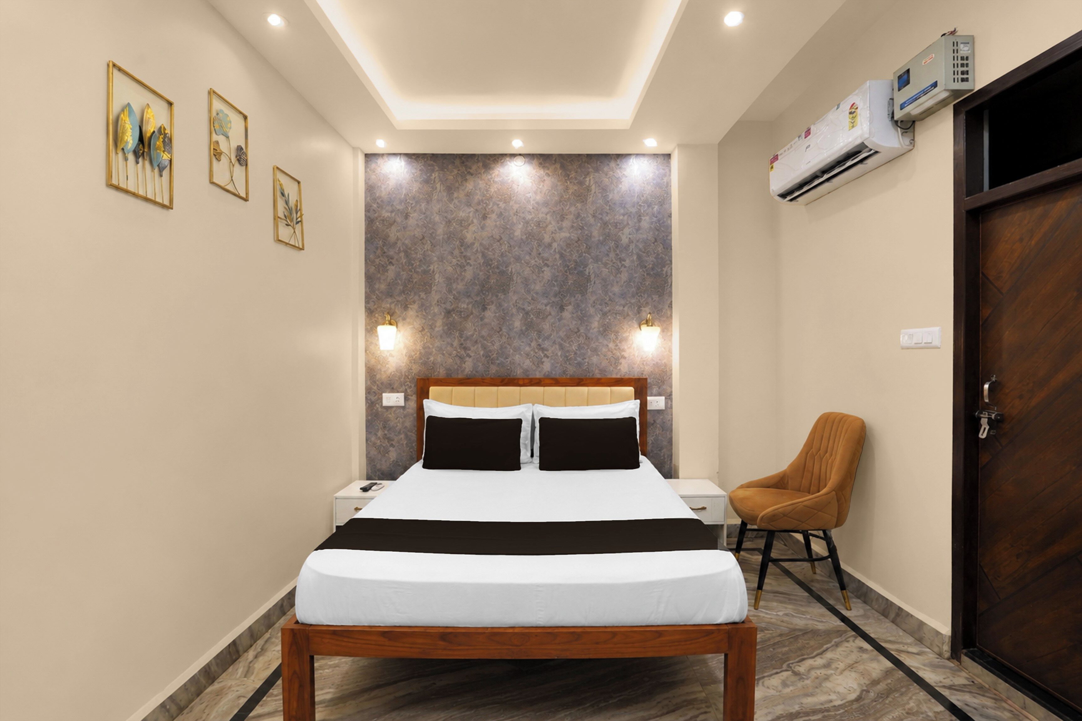 Quarto de hotel com cama, mesas de cabeceira, uma cadeira, aparelho de ar condicionado e porta.