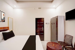 Quarto de hotel com cama, cadeira, televisão e guarda-roupa.