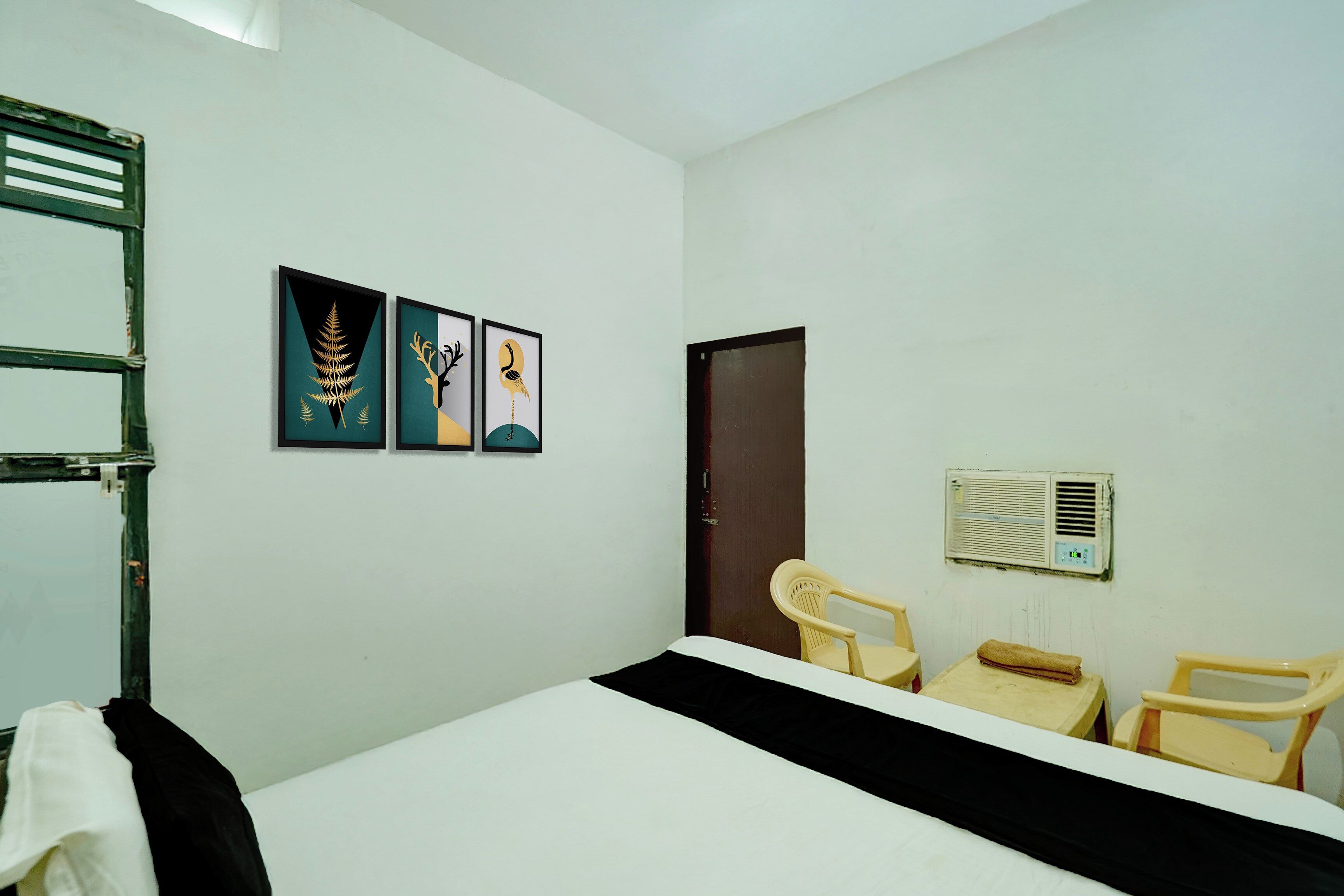 Quarto de hotel com uma cama, duas cadeiras, uma porta e três obras de arte emolduradas na parede.