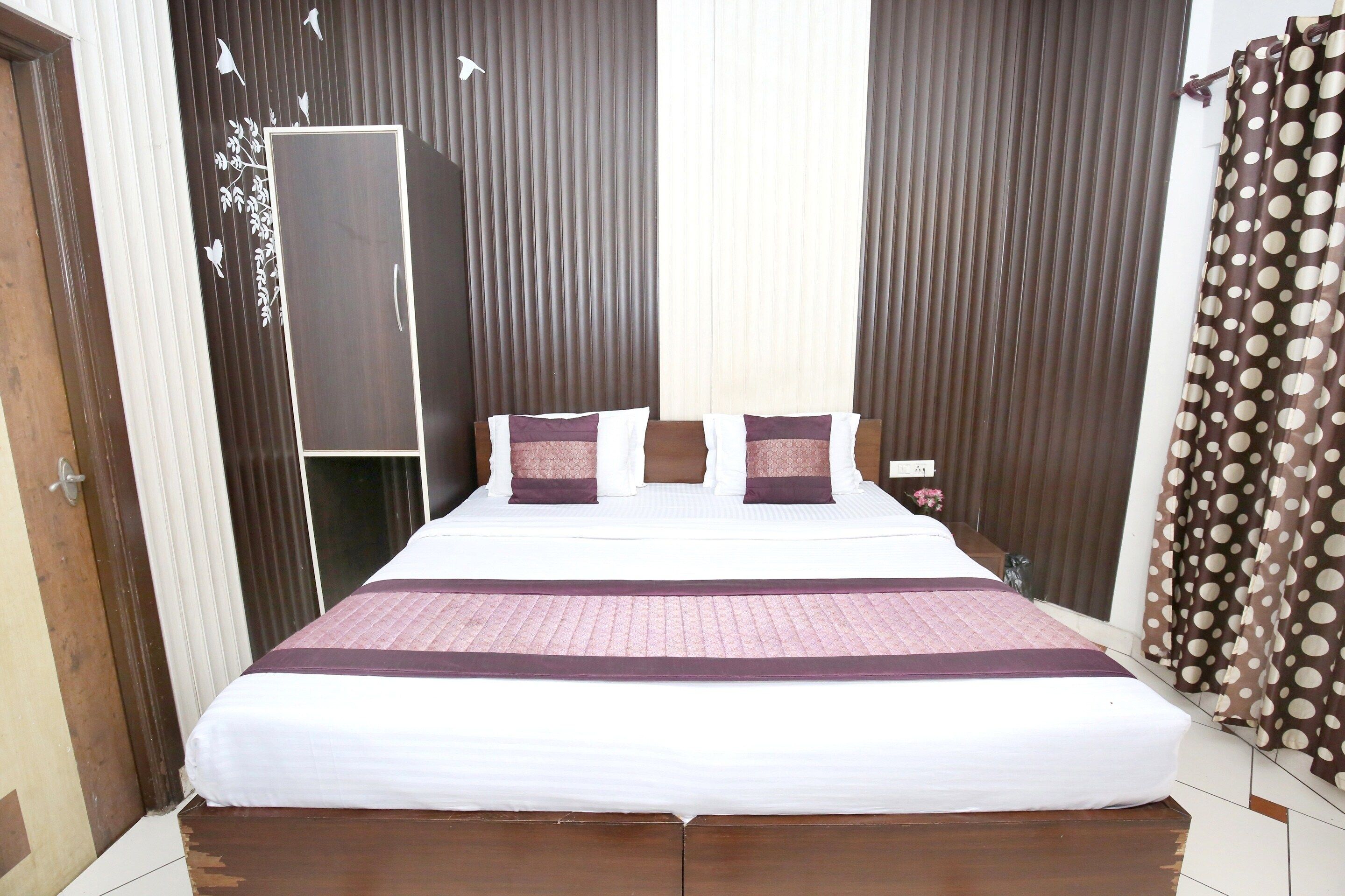 Quarto com uma cama grande, duas almofadas, mesa de cabeceira e cortina estampada em bolinhas.