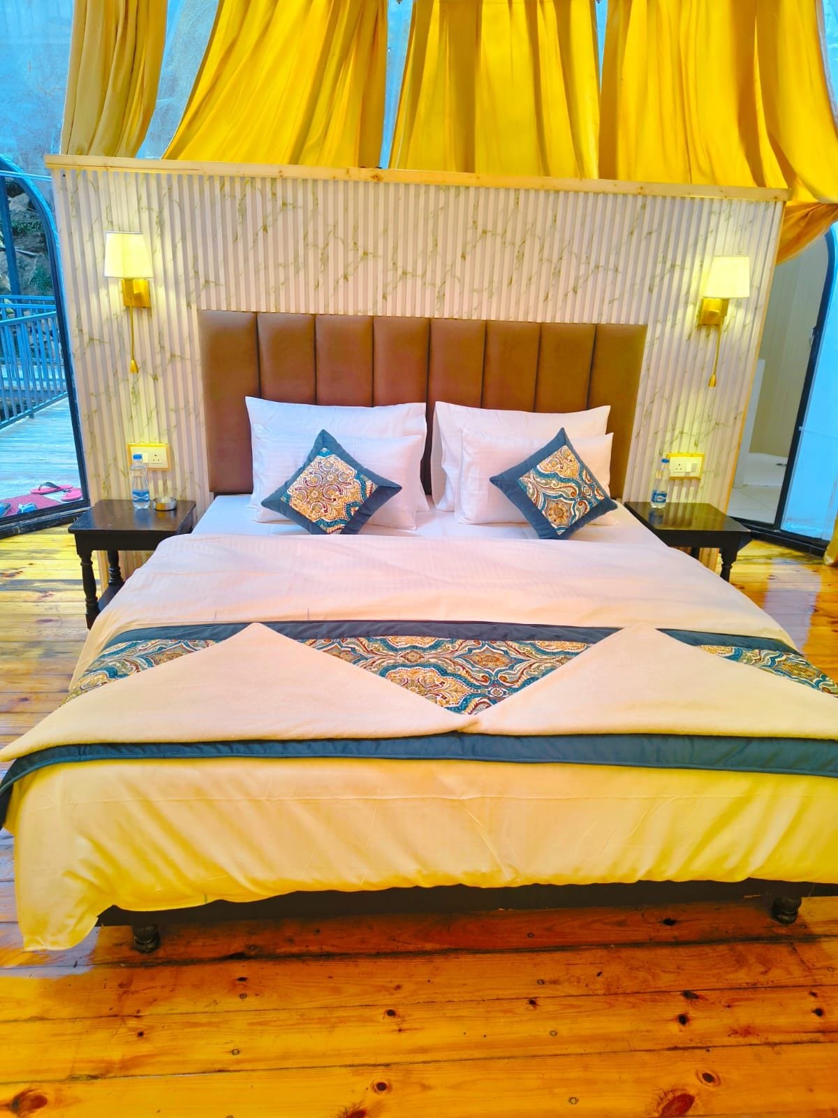 Uma cama com colcha estampada, cabeceira e duas luminárias de cabeceira.