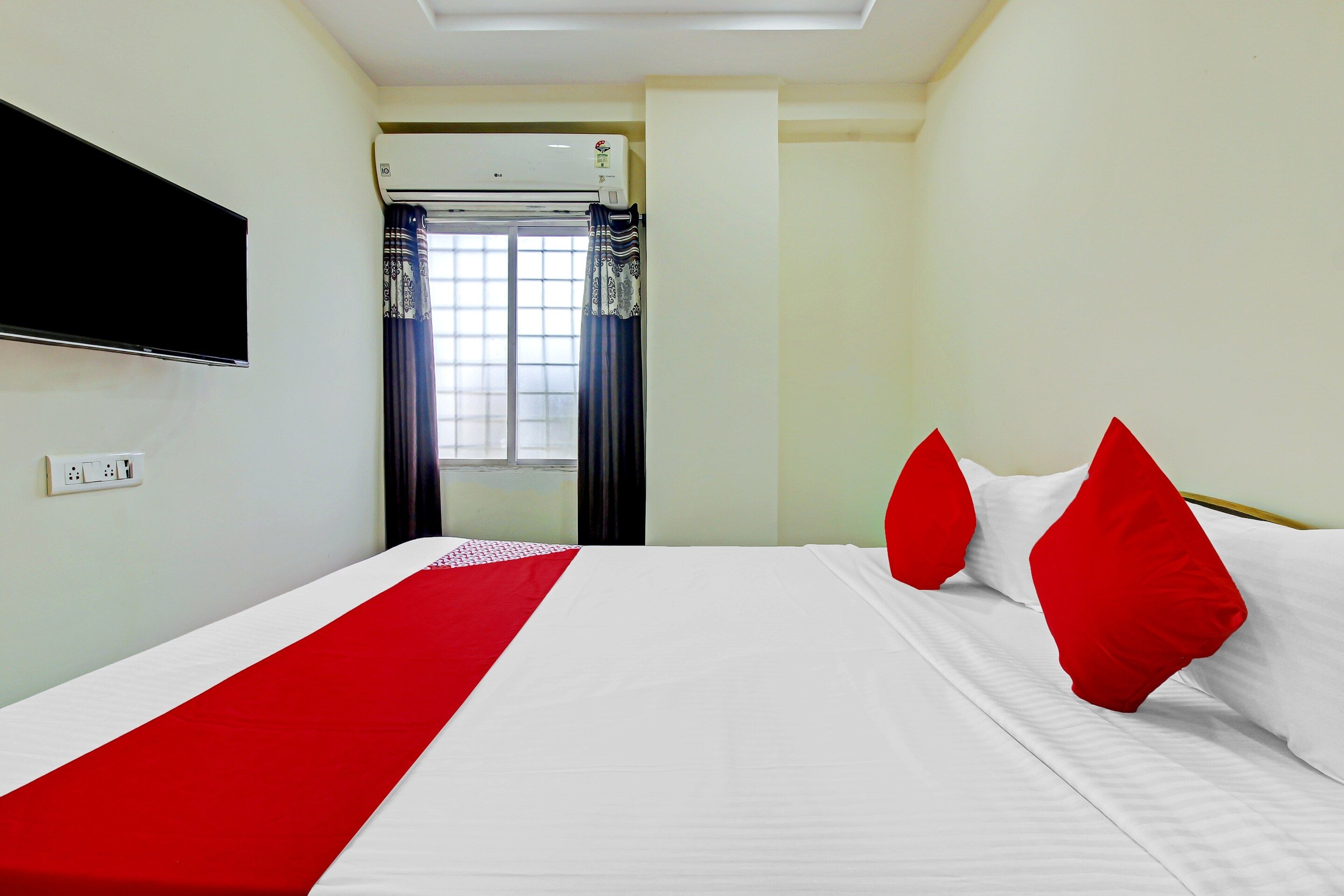 Quarto de hotel com cama, televisão de tela plana na parede, janela com cortinas e ar condicionado.