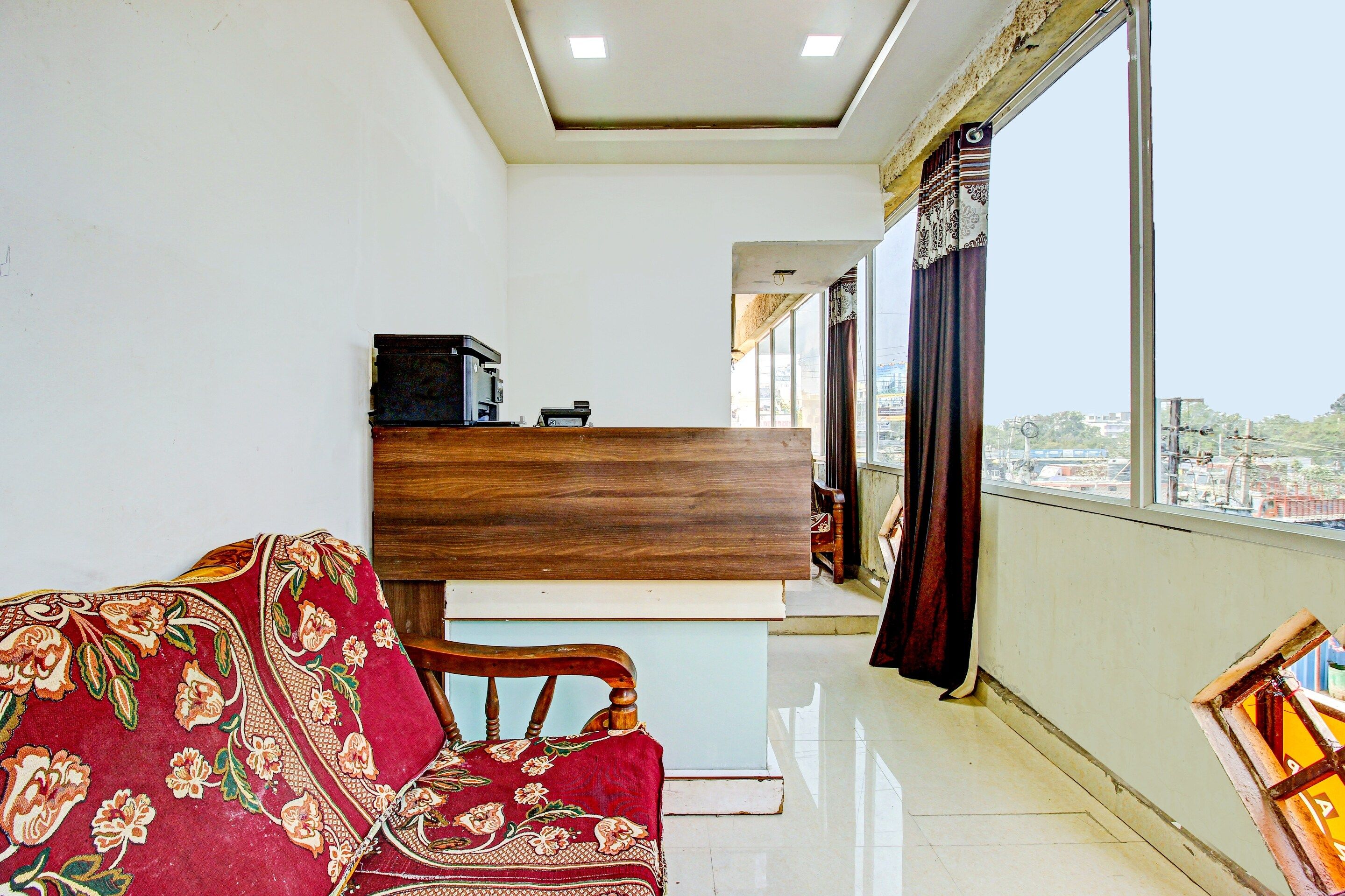 Quarto de hotel com uma mesa de recepção de madeira, um sofá vermelho e uma grande janela com cortinas.