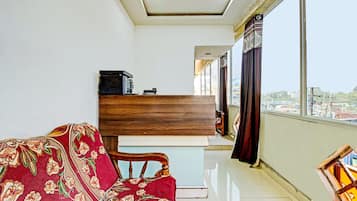 Quarto de hotel com uma mesa de recepção de madeira, um sofá vermelho e uma grande janela com cortinas.