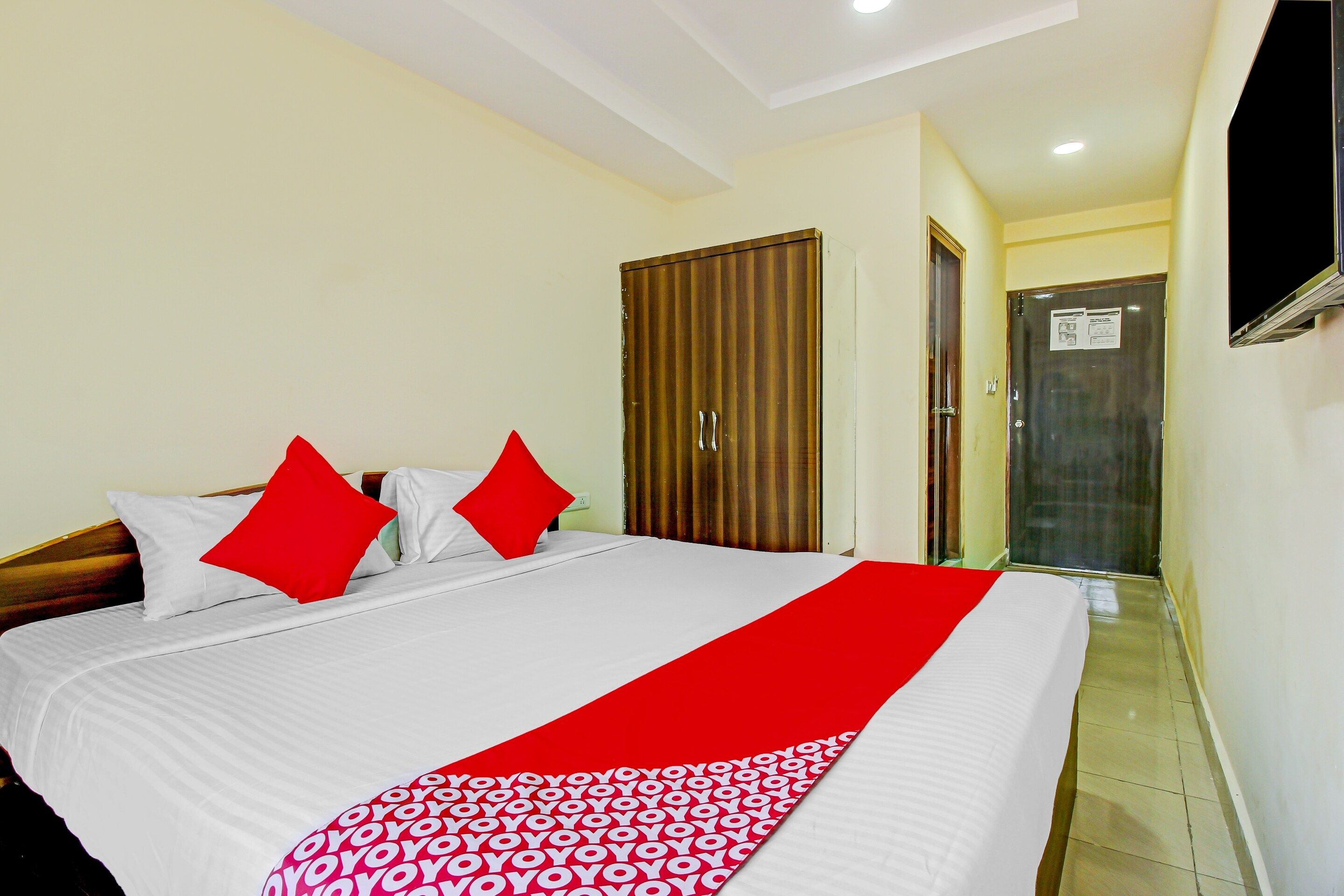 Quarto de hotel com cama, guarda-roupa, televisão e porta.