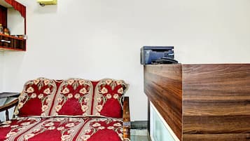 Quarto com escrivaninha de madeira, sofá vermelho estampado e luminária fixada na parede.