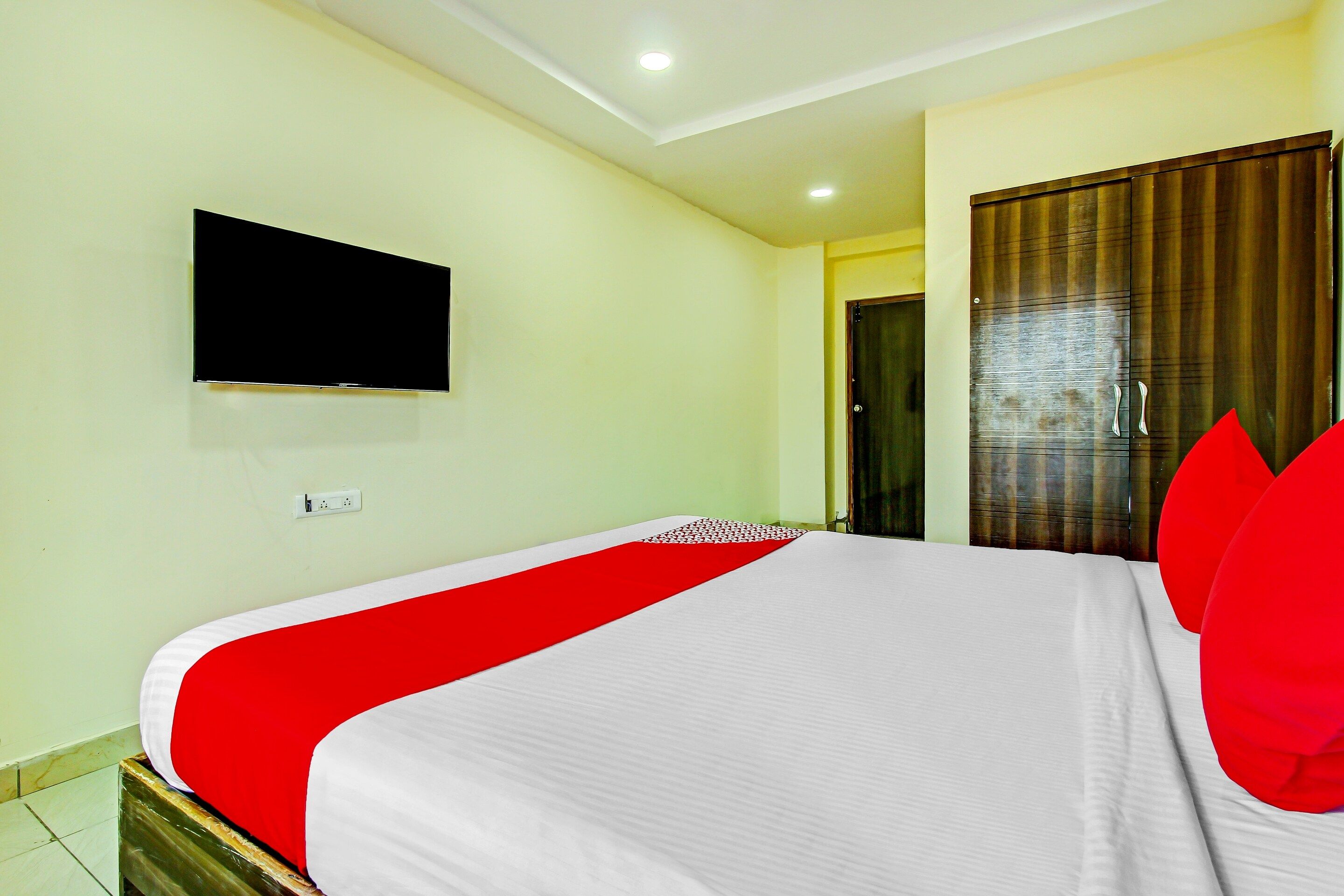 Quarto de hotel com cama, televisão fixada na parede e porta com janela.