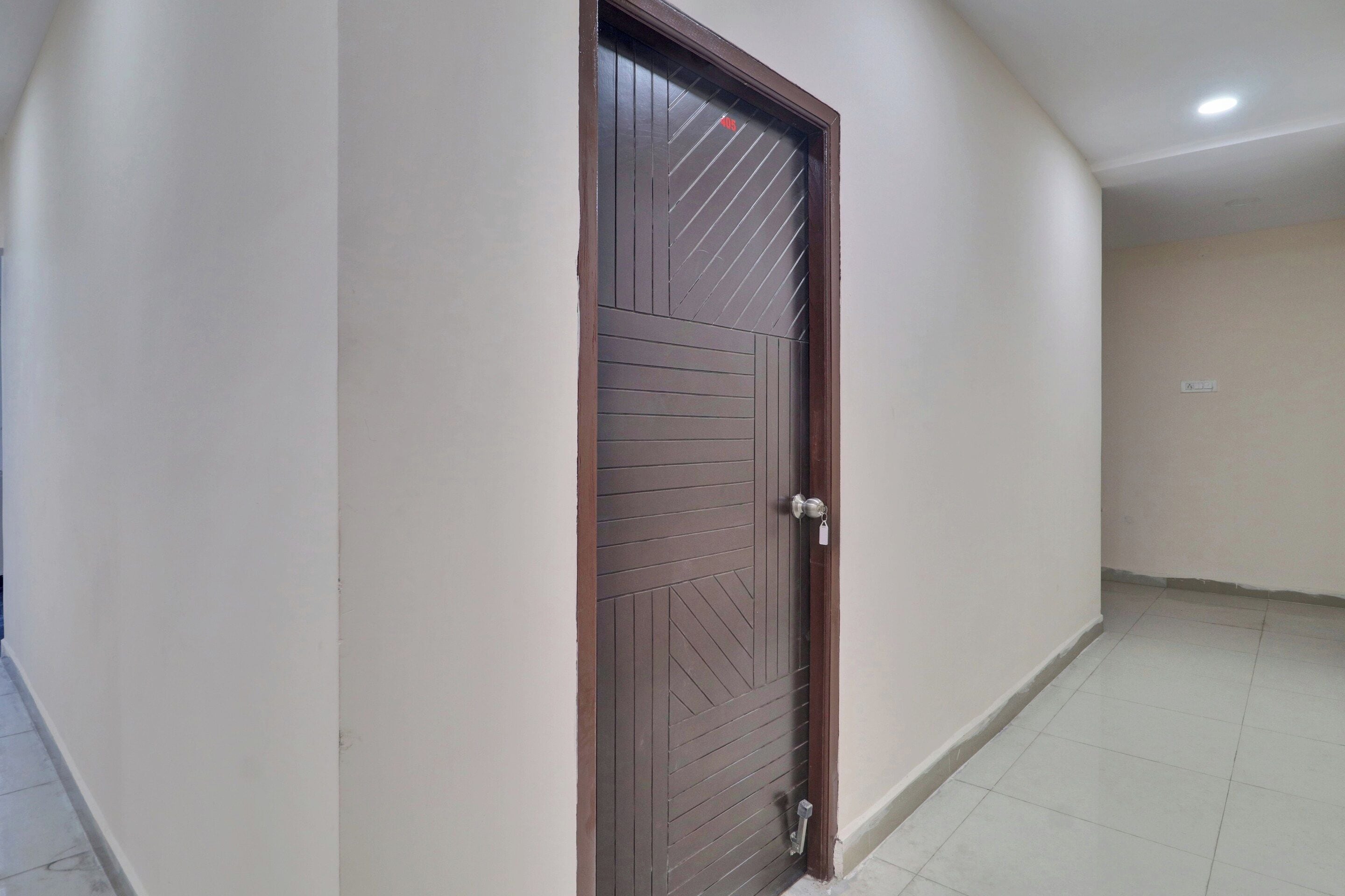 Uma porta fechada com olho de fechadura e maçaneta, um interruptor na parede e chão de azulejos.