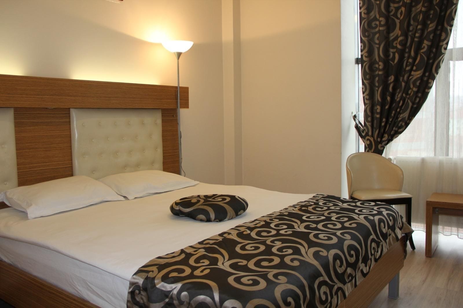 Quarto de hotel com uma cama, uma cadeira e um abajur.