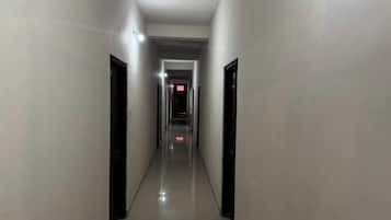 Um corredor comprido e estreito, com portas em ambos os lados e uma fonte de luz no final.