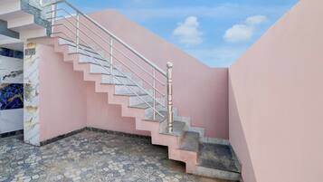 Escadaria com corrimão de metal que leva a um patamar, cercada por paredes cor-de-rosa e um piso de azulejos.