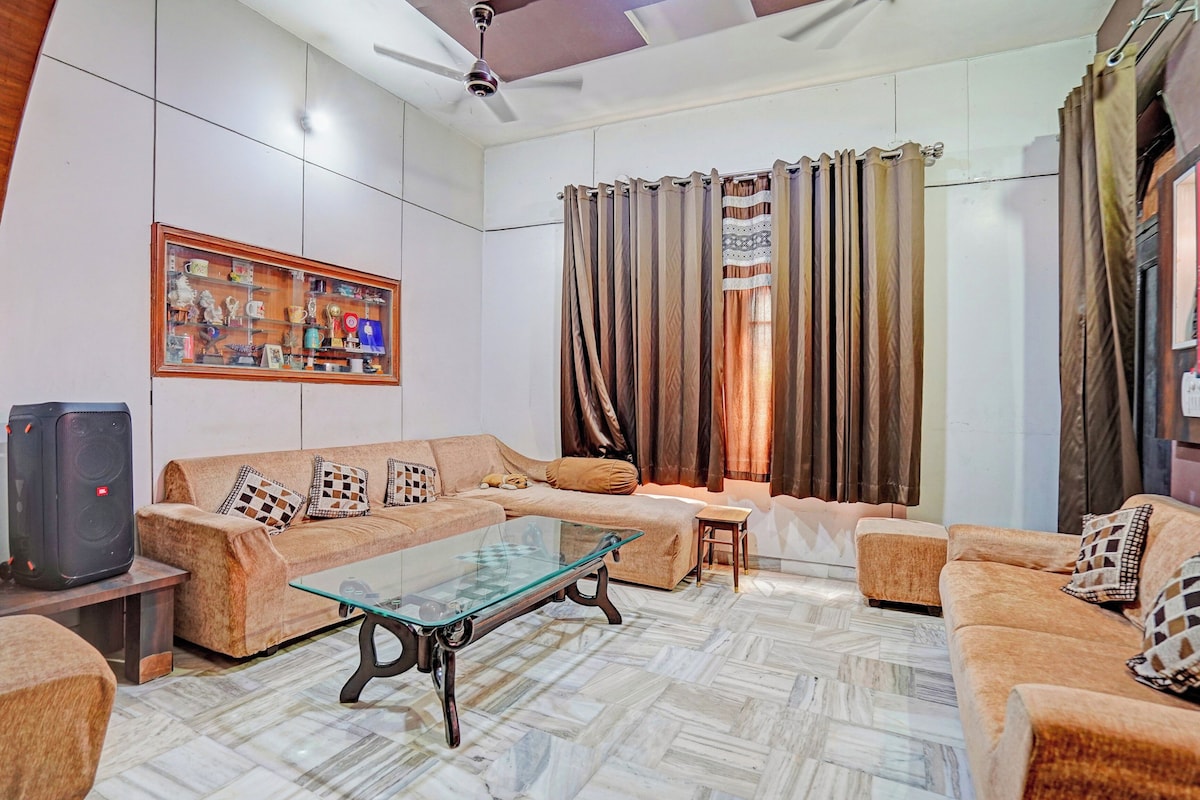 Sala de estar com sofá, mesa de centro de vidro, ventilador de teto e janela com cortinas.