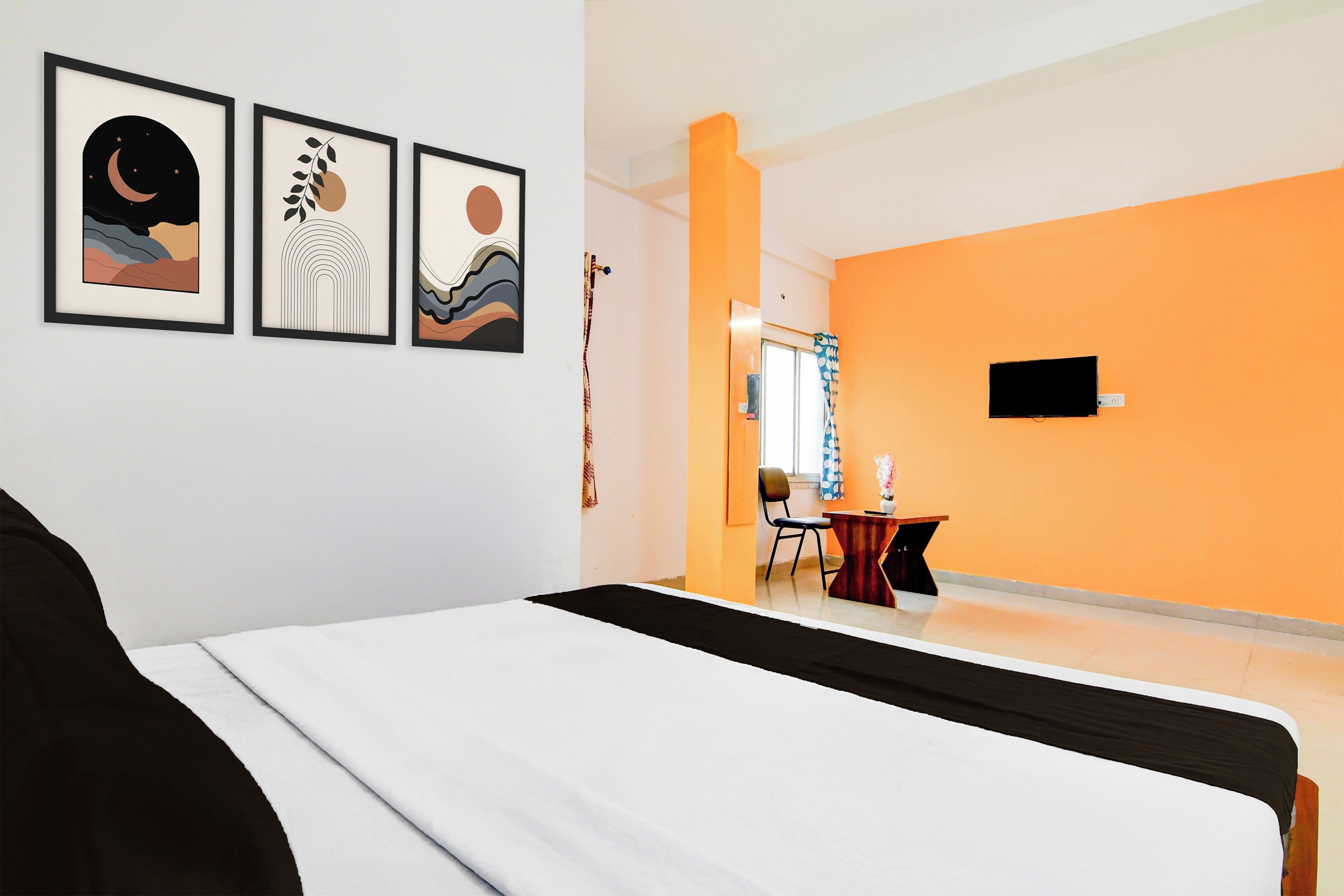 Quarto de hotel com cama, escrivaninha e televisão na parede.