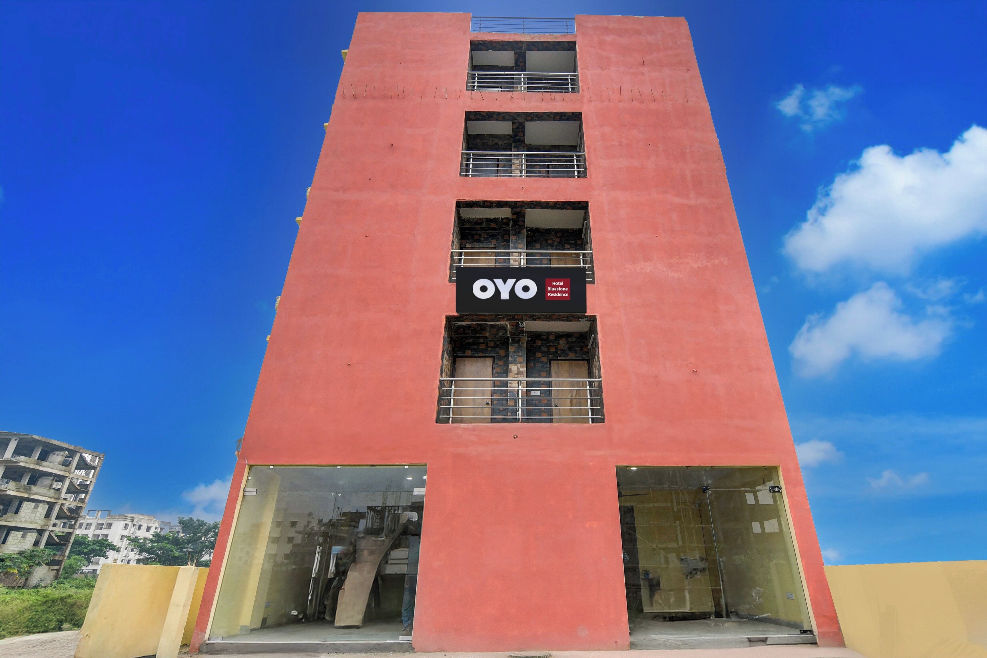 Um edifício vermelho com uma placa indicando 'OYO Hotel Bluestone Residence' e amplas janelas de vidro.