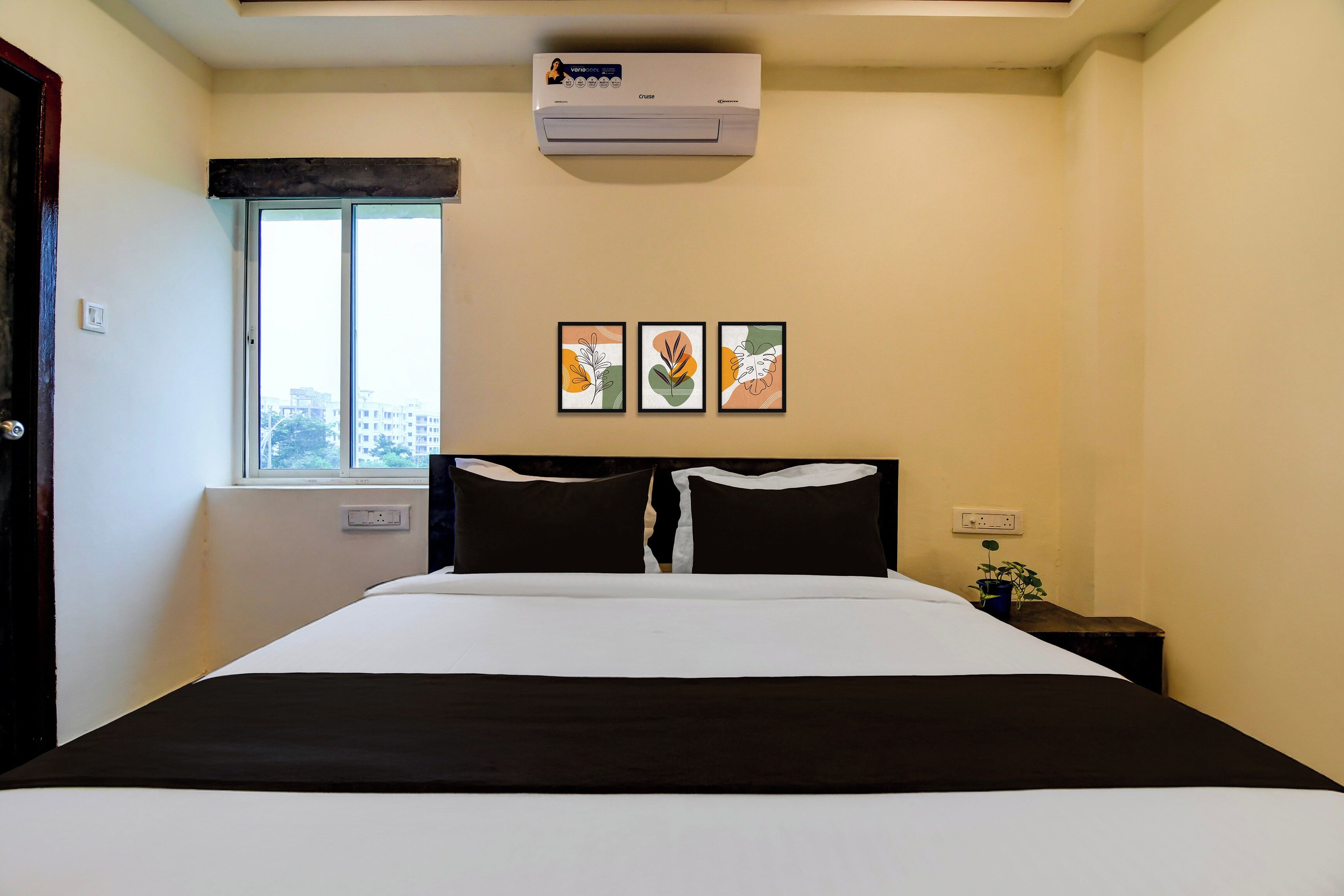 Quarto de hotel com cama, ar condicionado, janela com vista e três obras de arte emolduradas na parede.