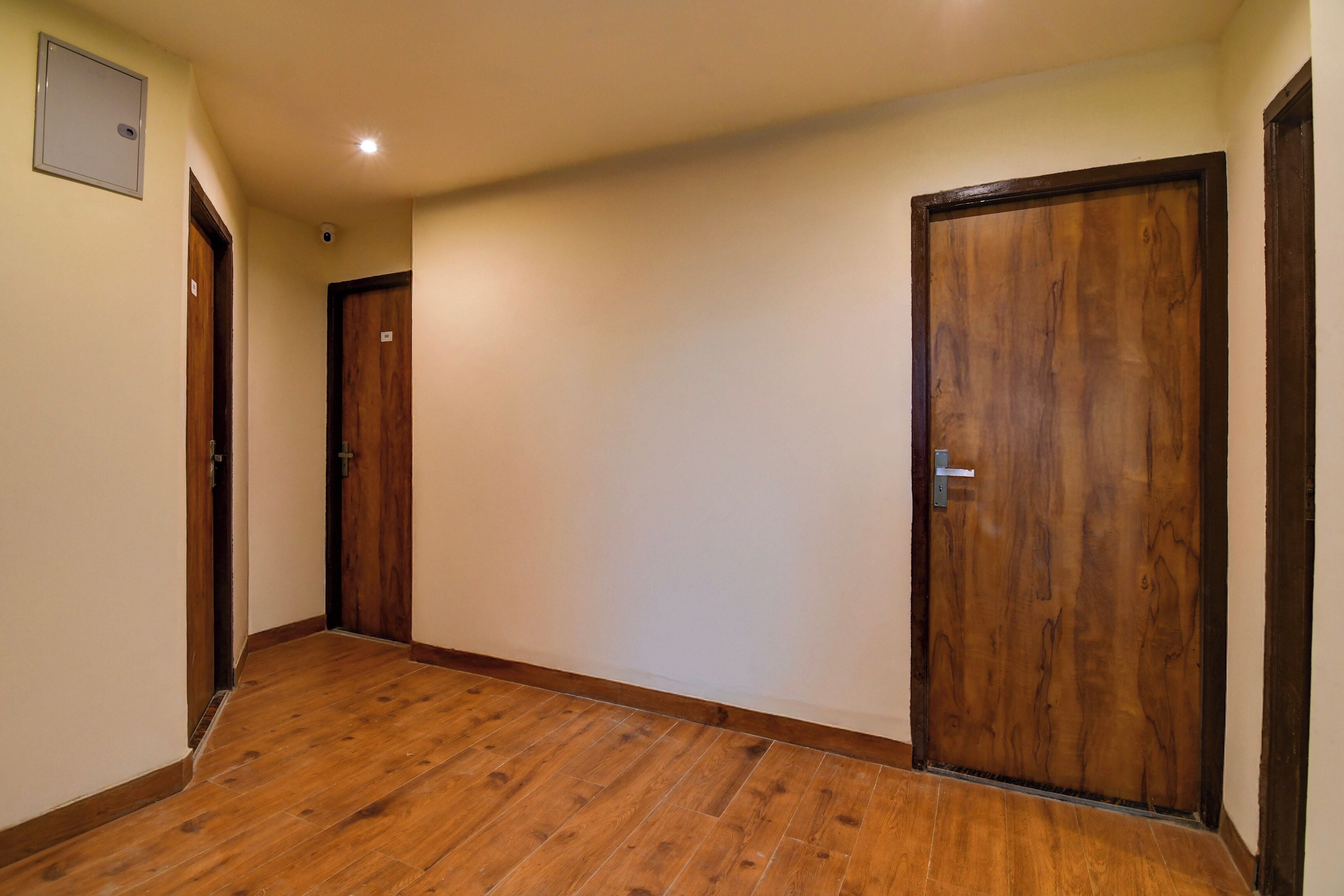 Um corredor com piso de madeira, duas portas de madeira e uma luminária no teto.