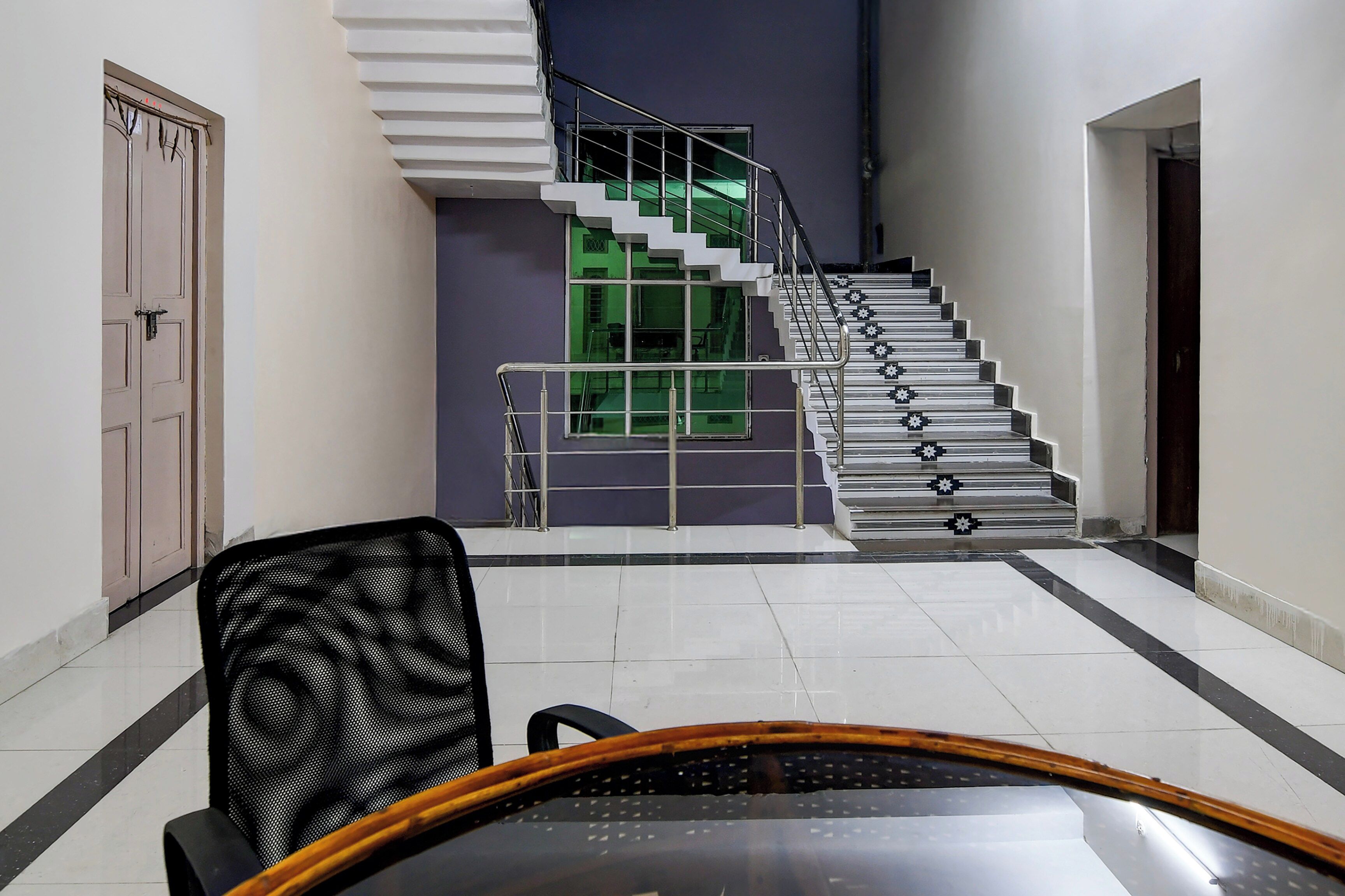 Uma escada com guarda-corrimão de metal, uma cadeira e uma porta em um corredor.