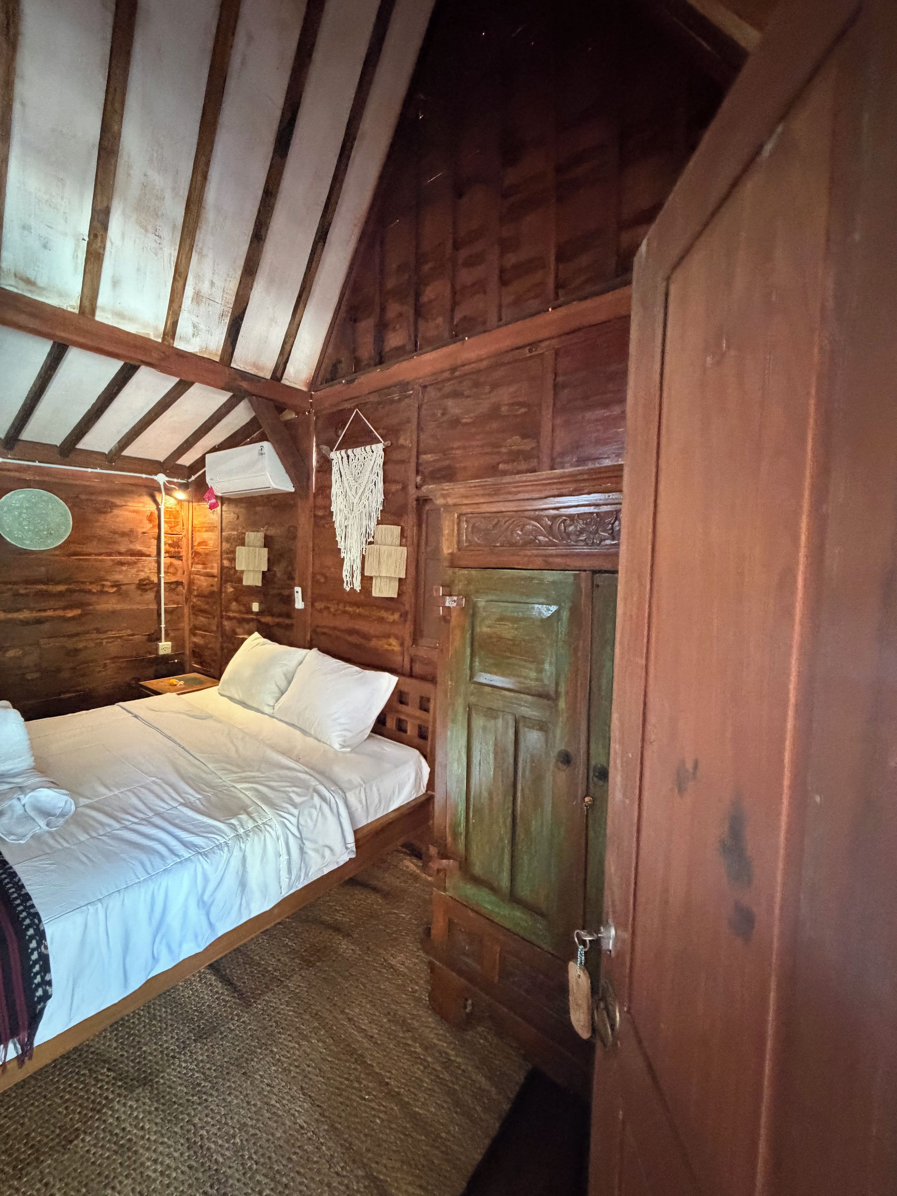 Quarto de madeira com cama, um enfeite de crochê pendurado na parede e uma porta verde.