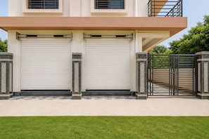 Um edifício moderno de dois andares com telhado plano, duas portas de garagem e entrada com portão.