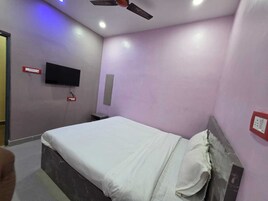 Quarto de hotel com cama, ventoinha no teto, televisão fixada na parede e placa de saída de emergência vermelha.