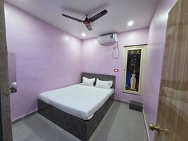 Quarto com cama, ventilador de teto, ar condicionado, porta e interruptor de luz fixado na parede.