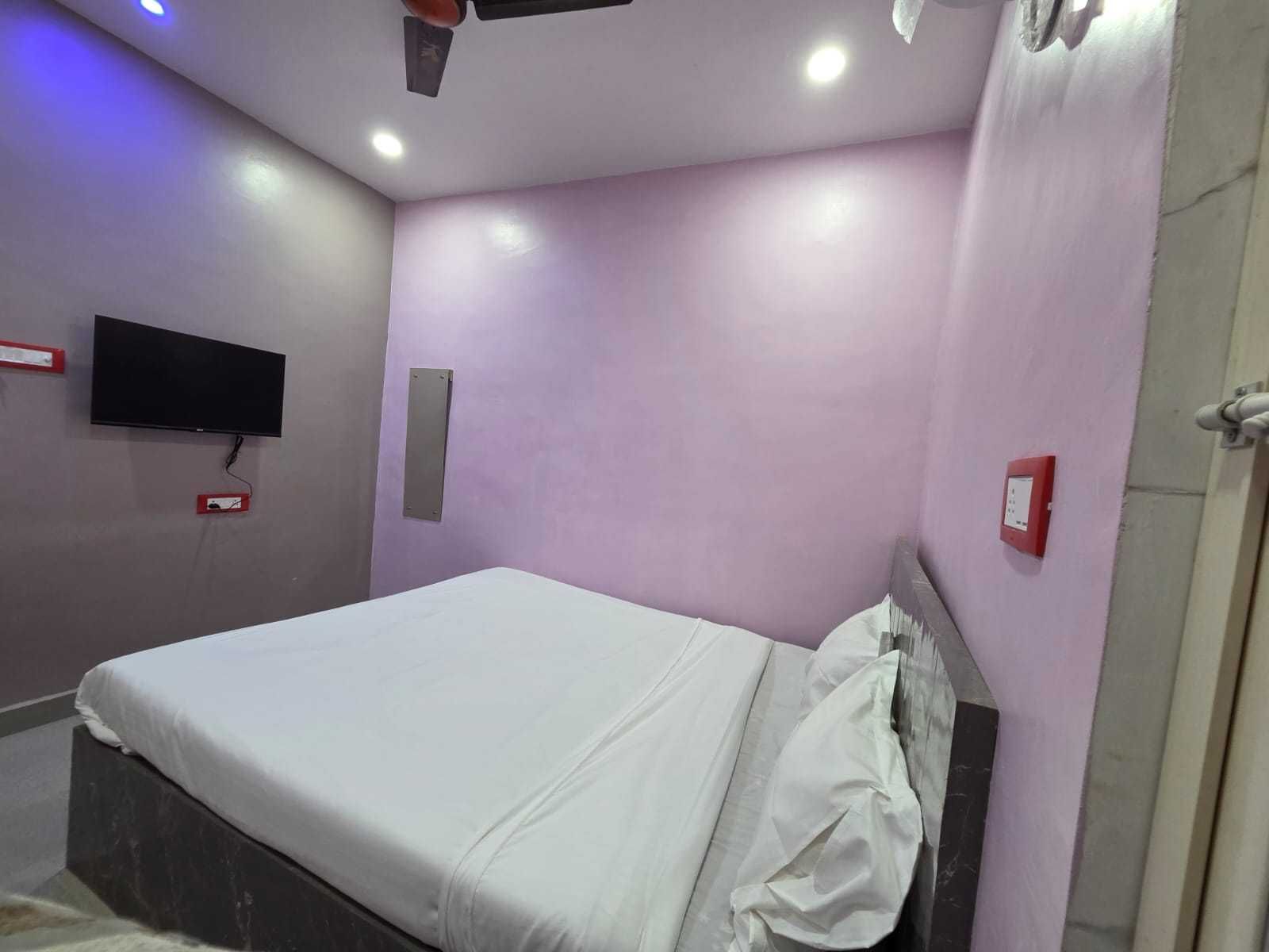 Quarto de hotel com uma cama, uma TV de tela plana na parede e um telefone de emergência vermelho.