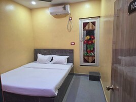 Quarto de hotel com cama, janela com arranjo de flores, porta com número e aparelho de ar condicionado.