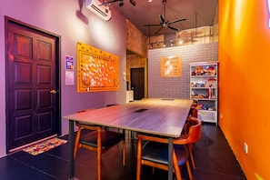 Quarto com mesa e cadeiras de madeira, uma parede com mensagens, uma estante e uma porta.