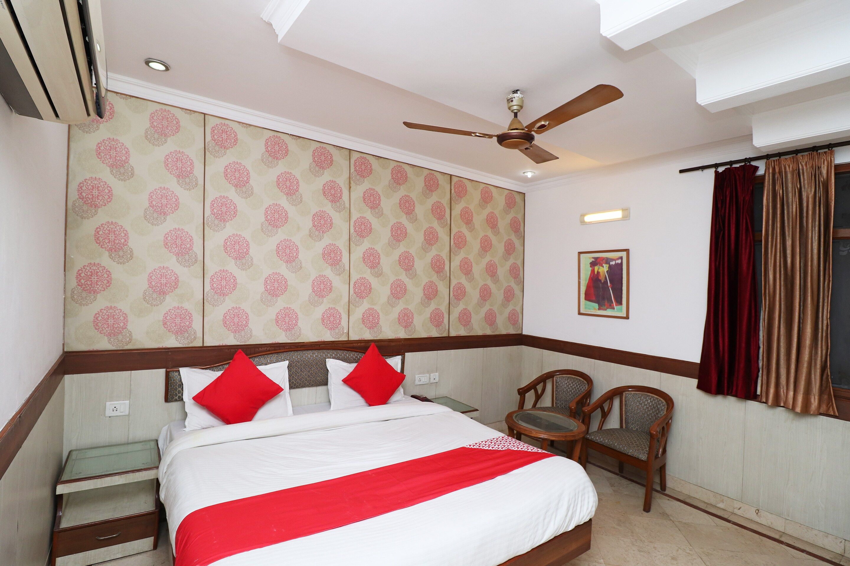 Quarto de hotel com cama, duas cadeiras, ventilador de teto e janela com cortinas.