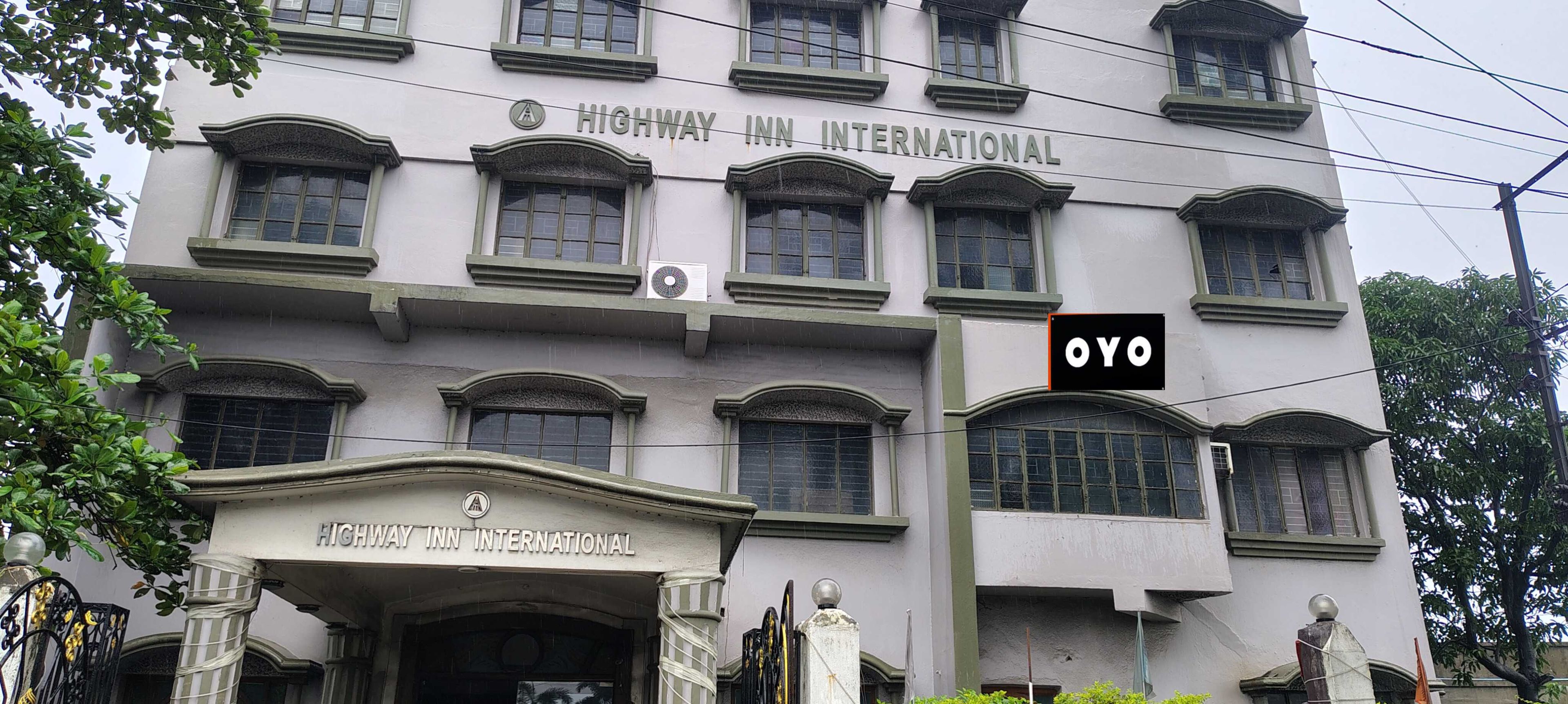 Um edifício com a placa 'HIGHWAY INN INTERNATIONAL' e uma placa menor 'OYO' na lateral.