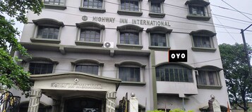 Um edifício com a placa 'HIGHWAY INN INTERNATIONAL' e uma placa menor 'OYO' na lateral.