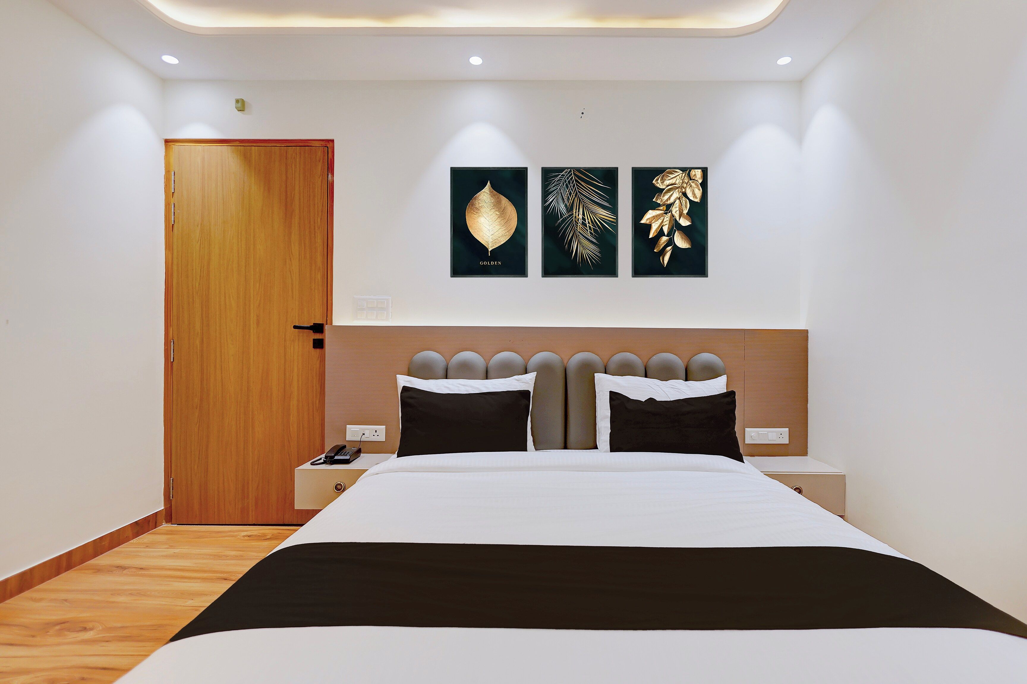 Quarto de hotel com cama, mesas de cabeceira, porta de madeira e obras de arte penduradas na parede.