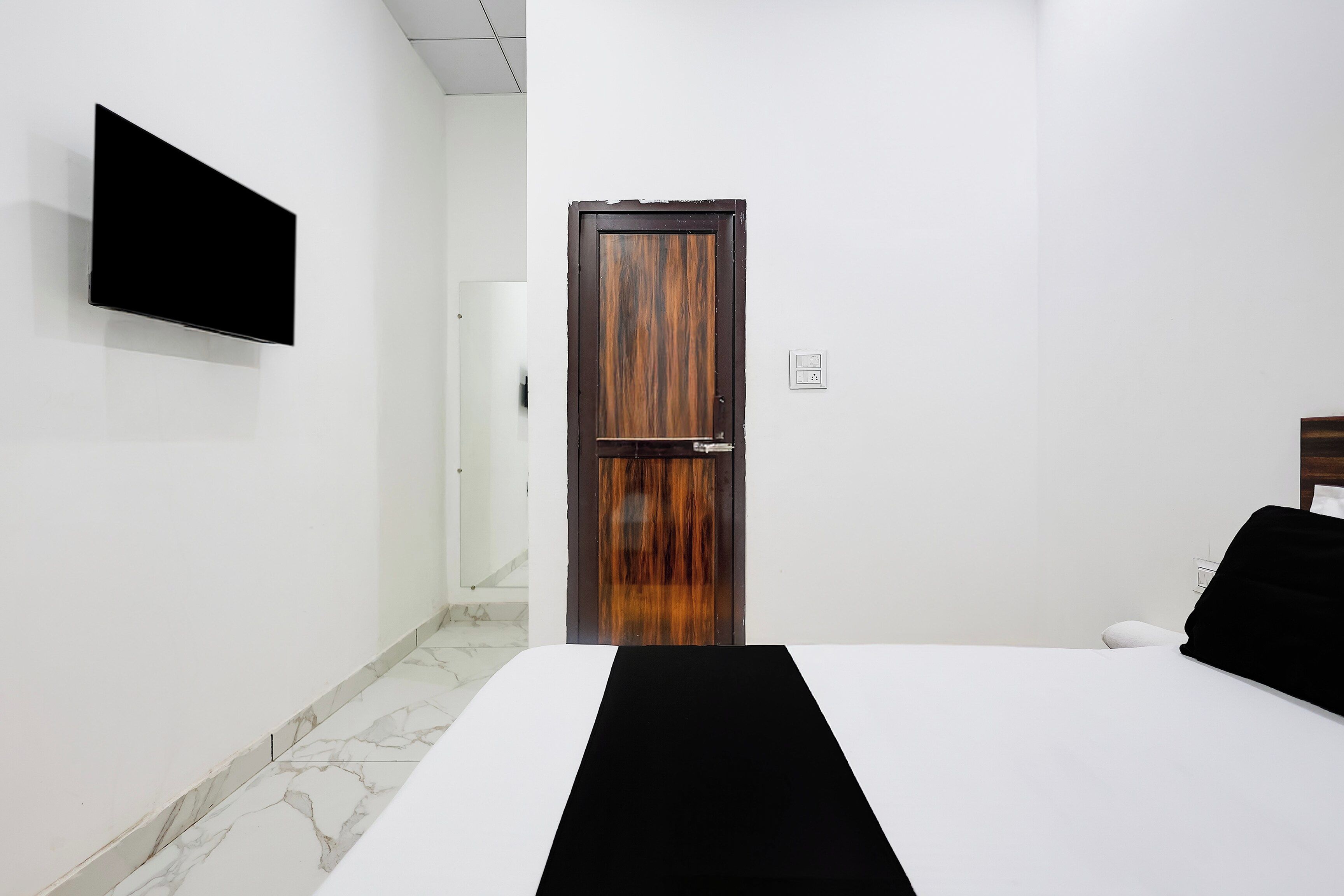 Quarto de hotel com cama, televisão de tela plana na parede, porta de madeira e piso de mármore.