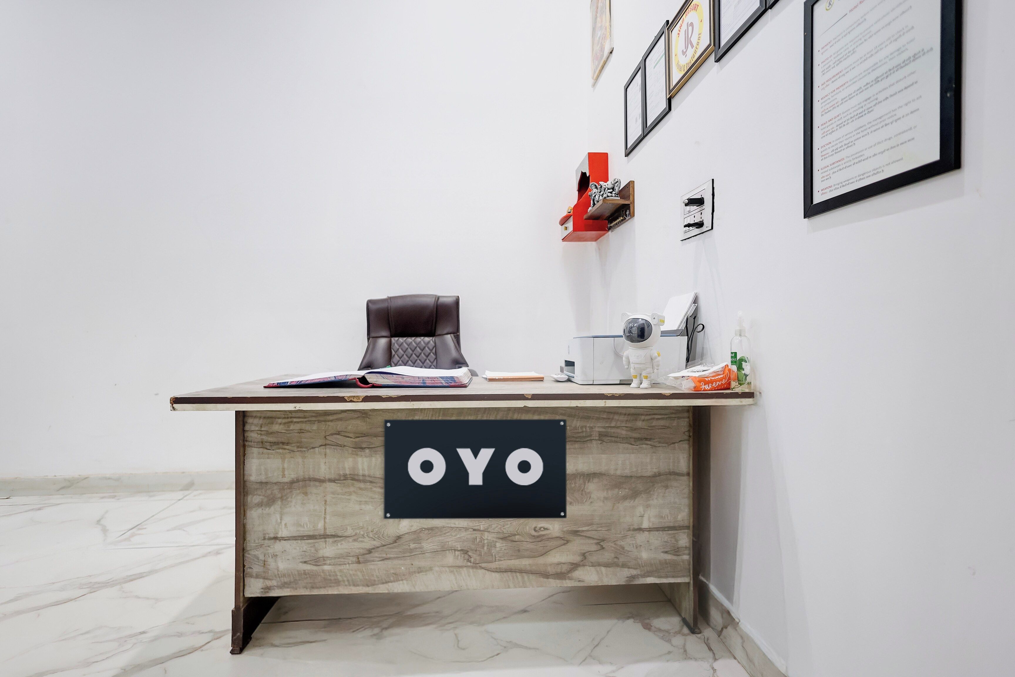 Uma mesa de madeira com uma placa indicando 'OYO' em um quarto com paredes brancas e piso de mármore.