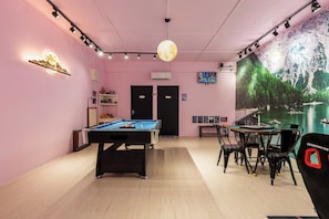 Quarto com mesa de bilhar, cadeiras, um grande mural e luminária no teto.